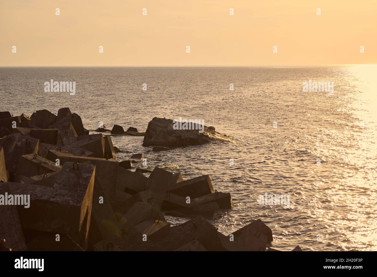 Seascape with large concrete breakwaters at beautiful orange sunset ...