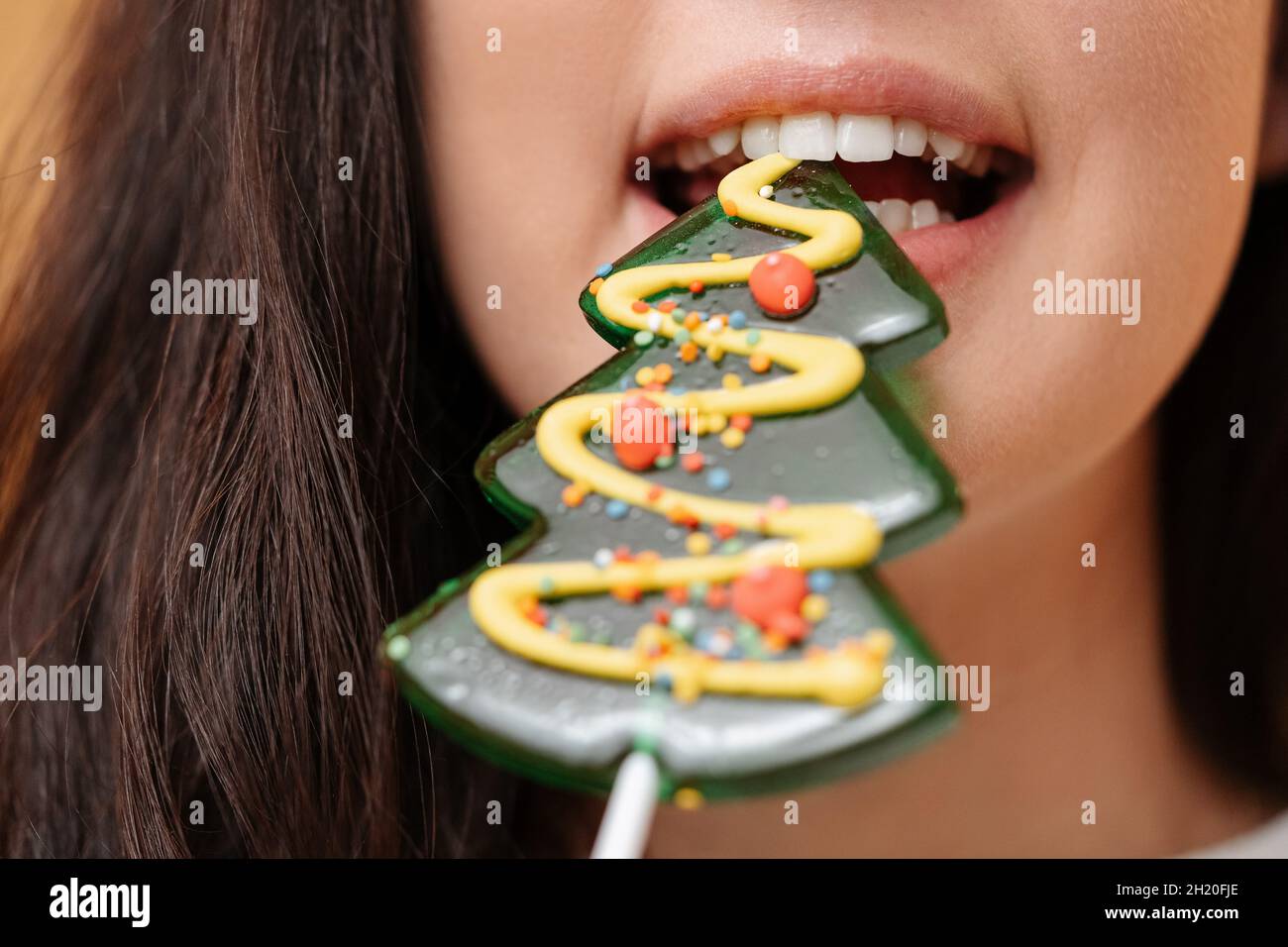 Woman biting off a Christmas tree lollipop with white healthy teeth ...