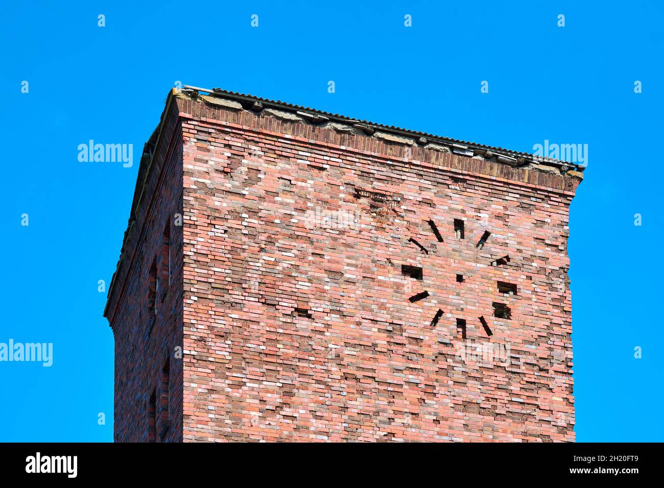Old abandoned red brick tower with round clock on facade against blue ...