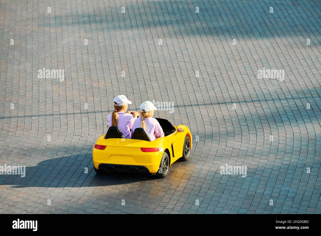 Two little girls driving yellow toy car on pavement in amusement park ...