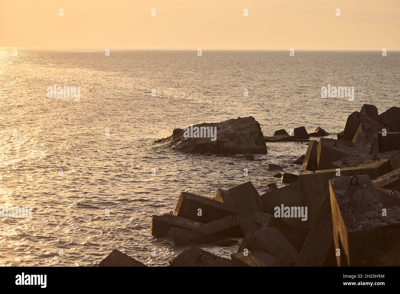 Seascape with large concrete breakwaters at beautiful orange sunset ...