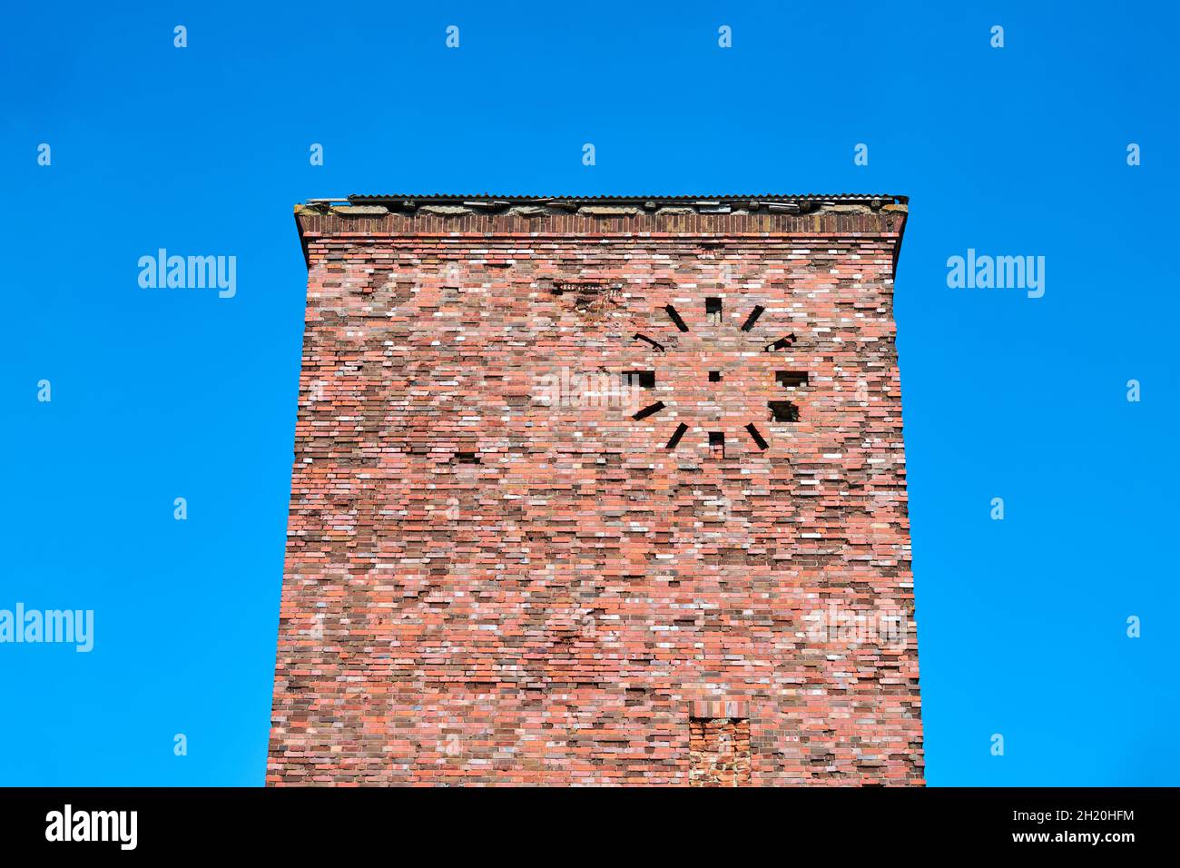 Old abandoned red brick tower with round clock on facade against blue ...