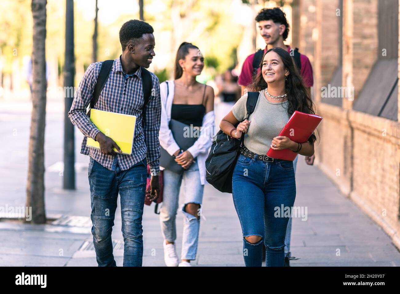 Four students of different ethnicities walking in outdoors with school ...