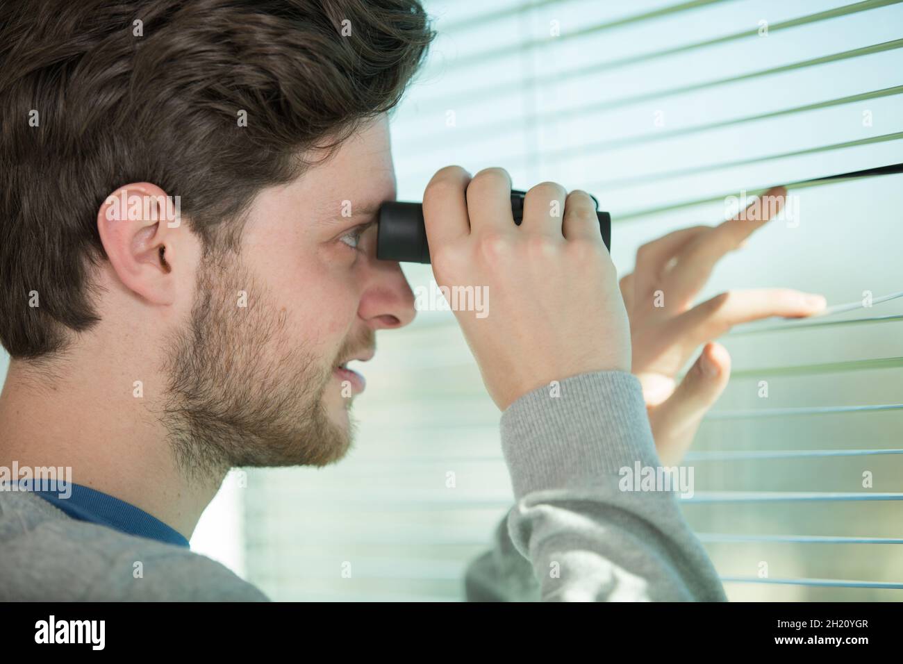 young man standing looking through a glass window with binoculars Stock ...