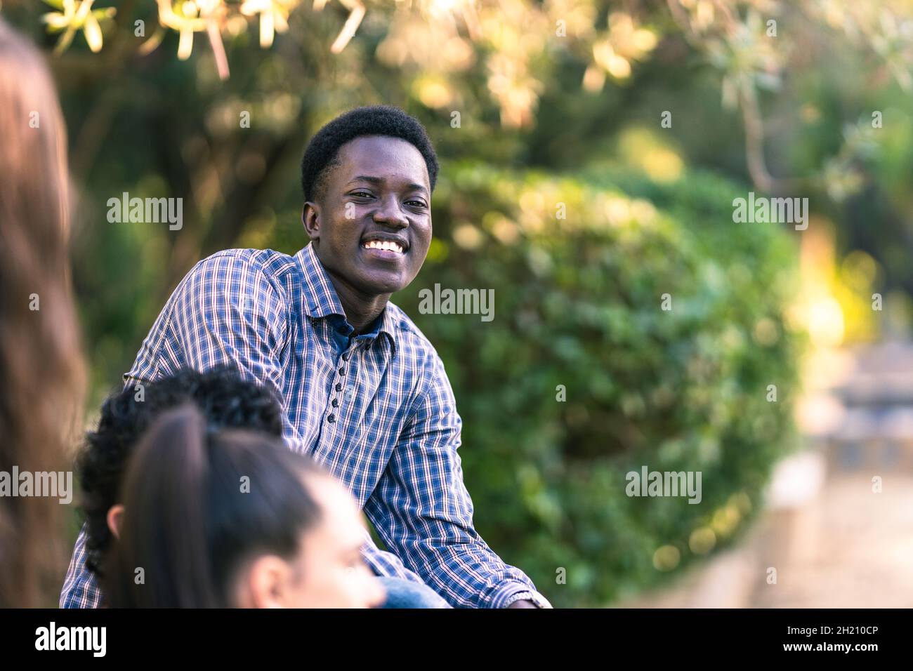 African man sitting on a bench next to a multiethnic group of friends ...