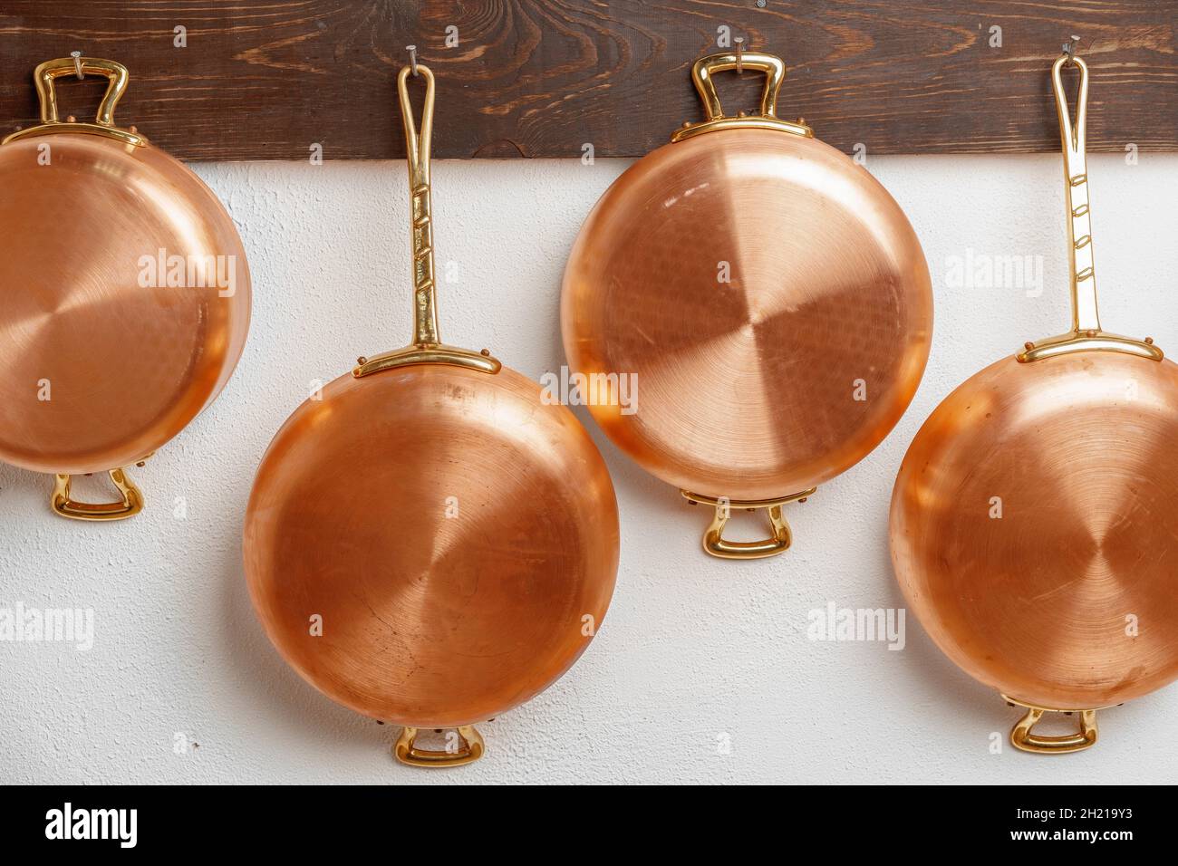 Row of shiny clean copper pans, different size, hung on wooden plank ...