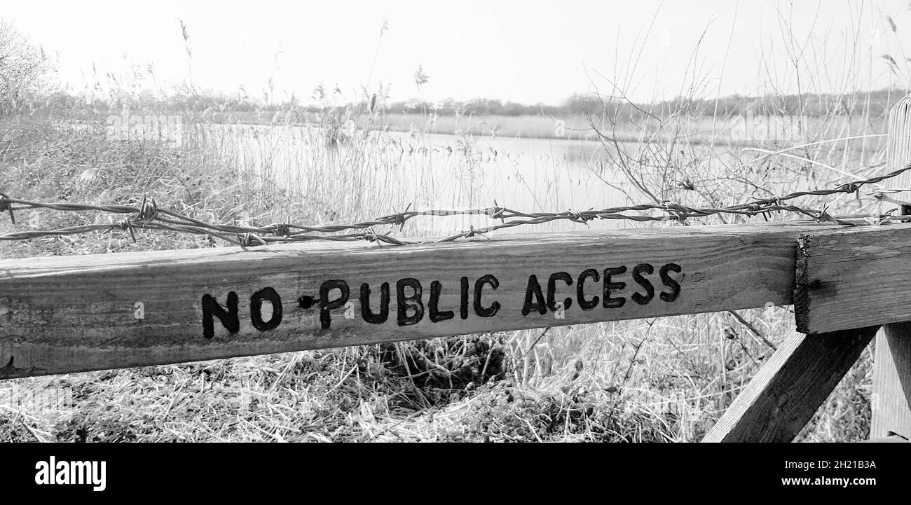 Grayscale panorama of a sign "NO PUBLIC ACCESS" written on a fence with ...
