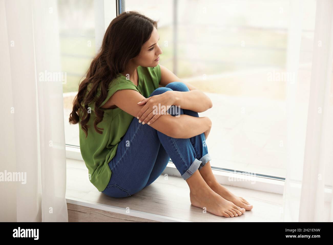 Young sad woman sitting near window at home Stock Photo - Alamy