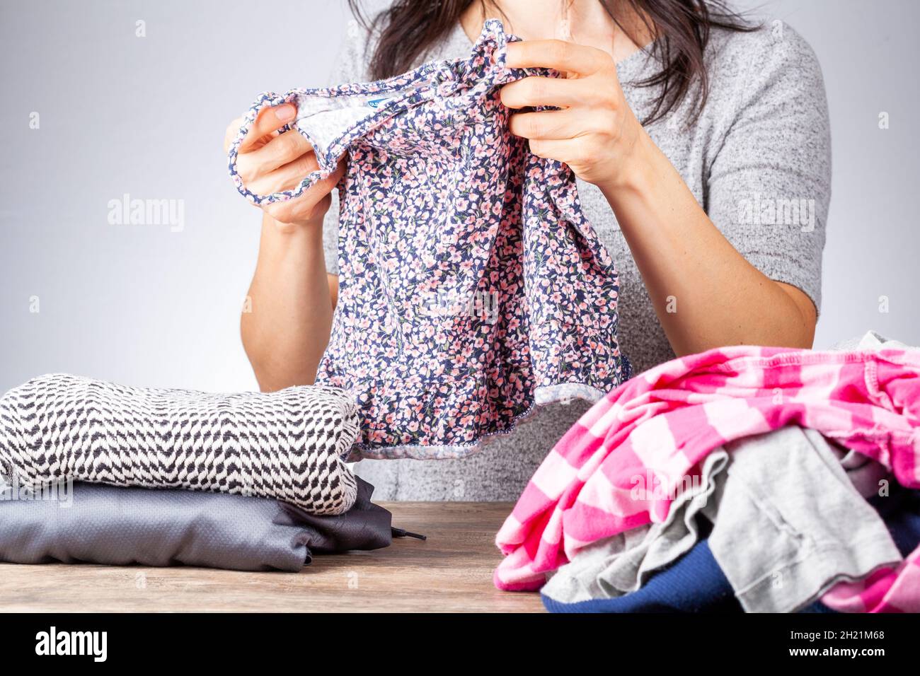 A caucasian woman is folding clean dresses on a wooden desk. There is a ...