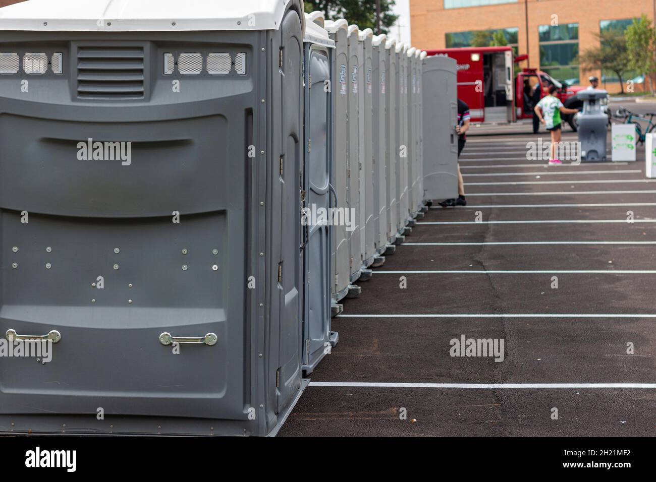 A line up of many grey portable toilets at a parking lot to be used by ...