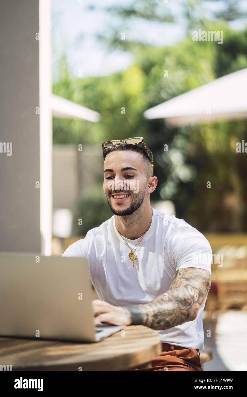 Vertical closeup of a young guy working on his laptop from outside ...