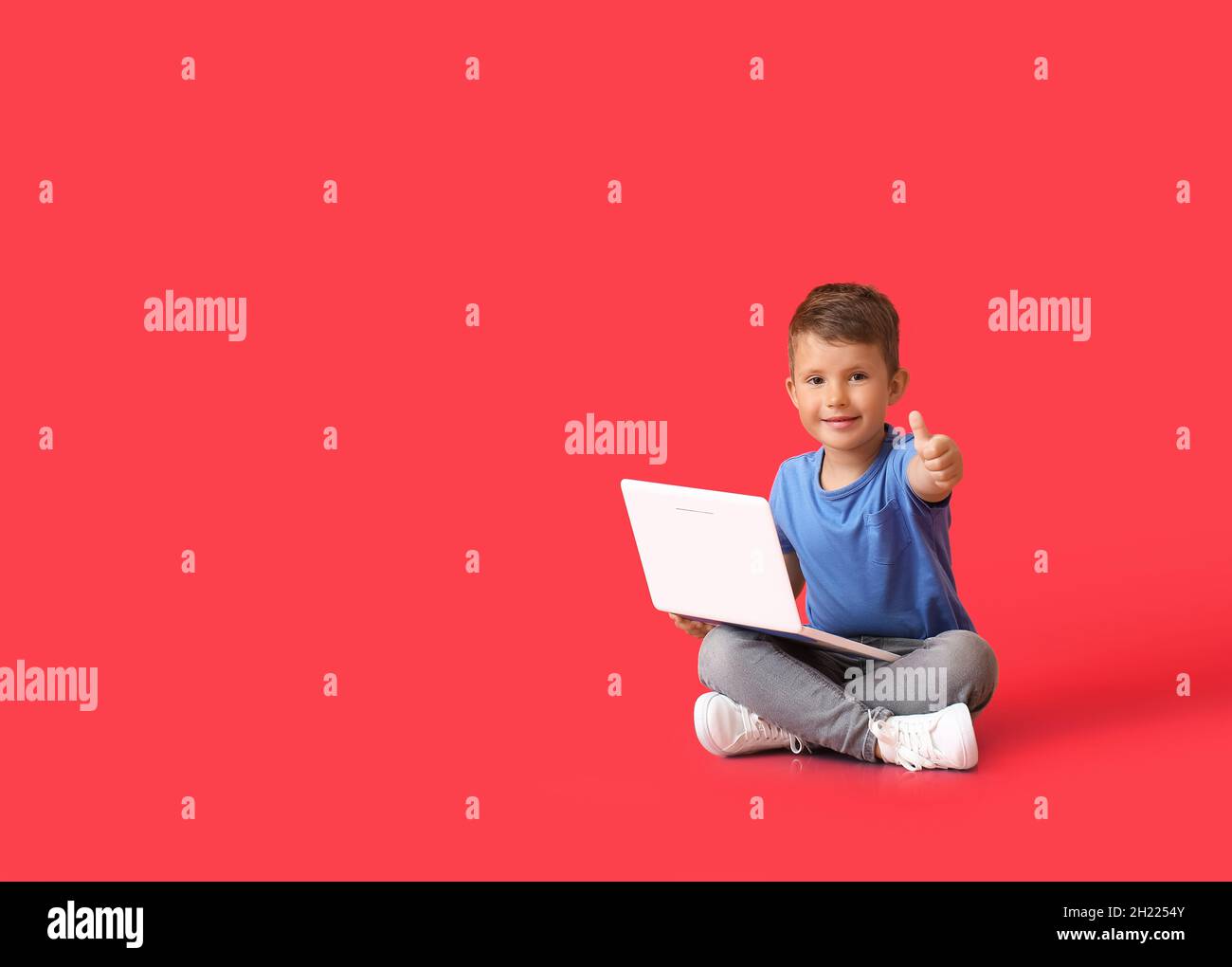 Cute little boy with laptop showing thumb-up on red background Stock ...