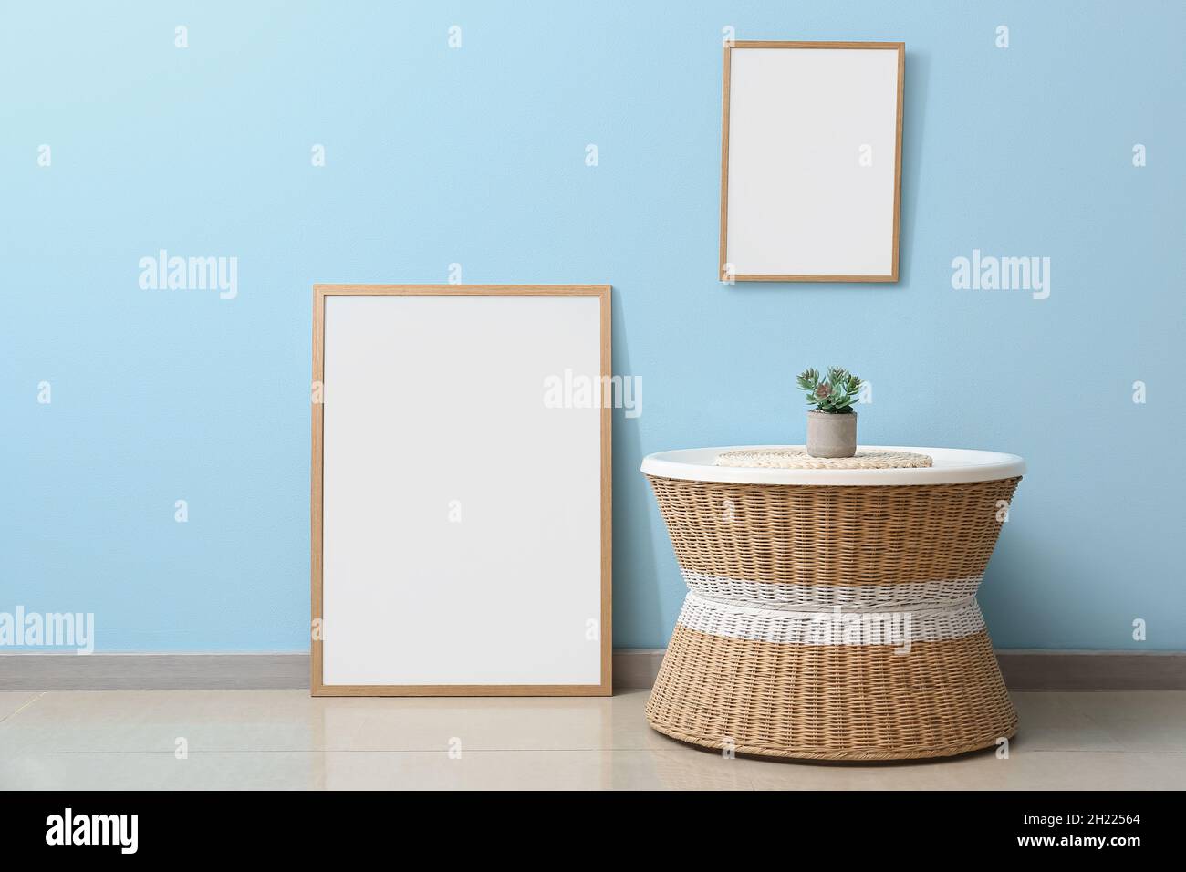 Rattan table and blank poster frames near color wall Stock Photo - Alamy