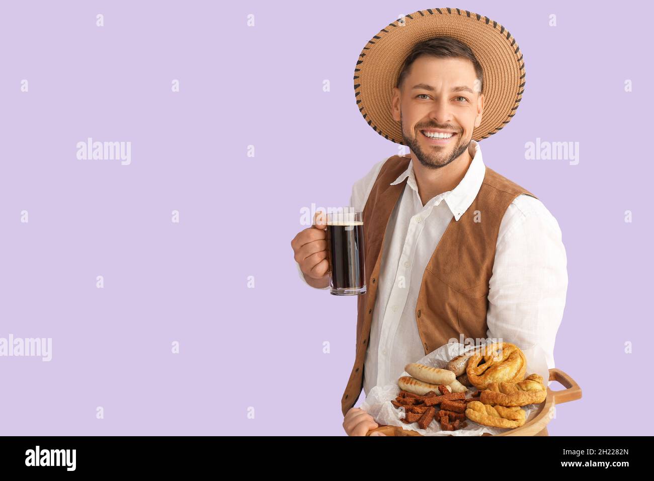 Young man in traditional German clothes with beer and food on lilac ...
