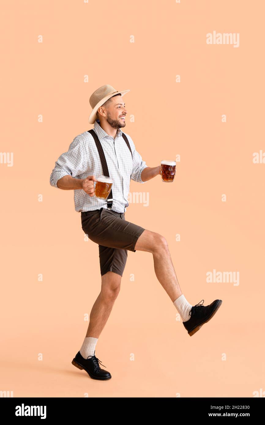 Young man in traditional German clothes with beer on beige background ...