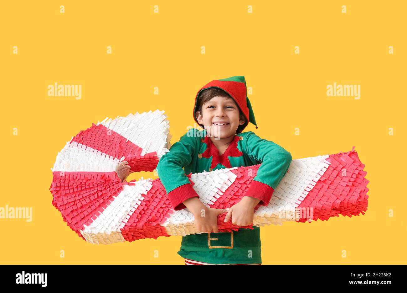 Cute little boy dressed as elf with candy cane pinata on color ...