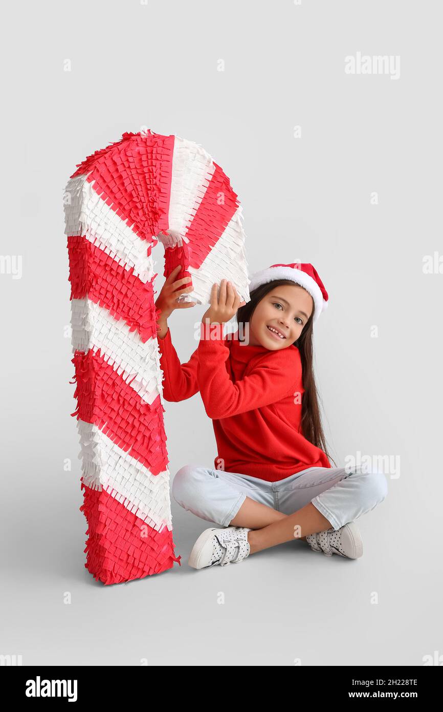 Little girl in Santa hat and with candy cane pinata on light background ...