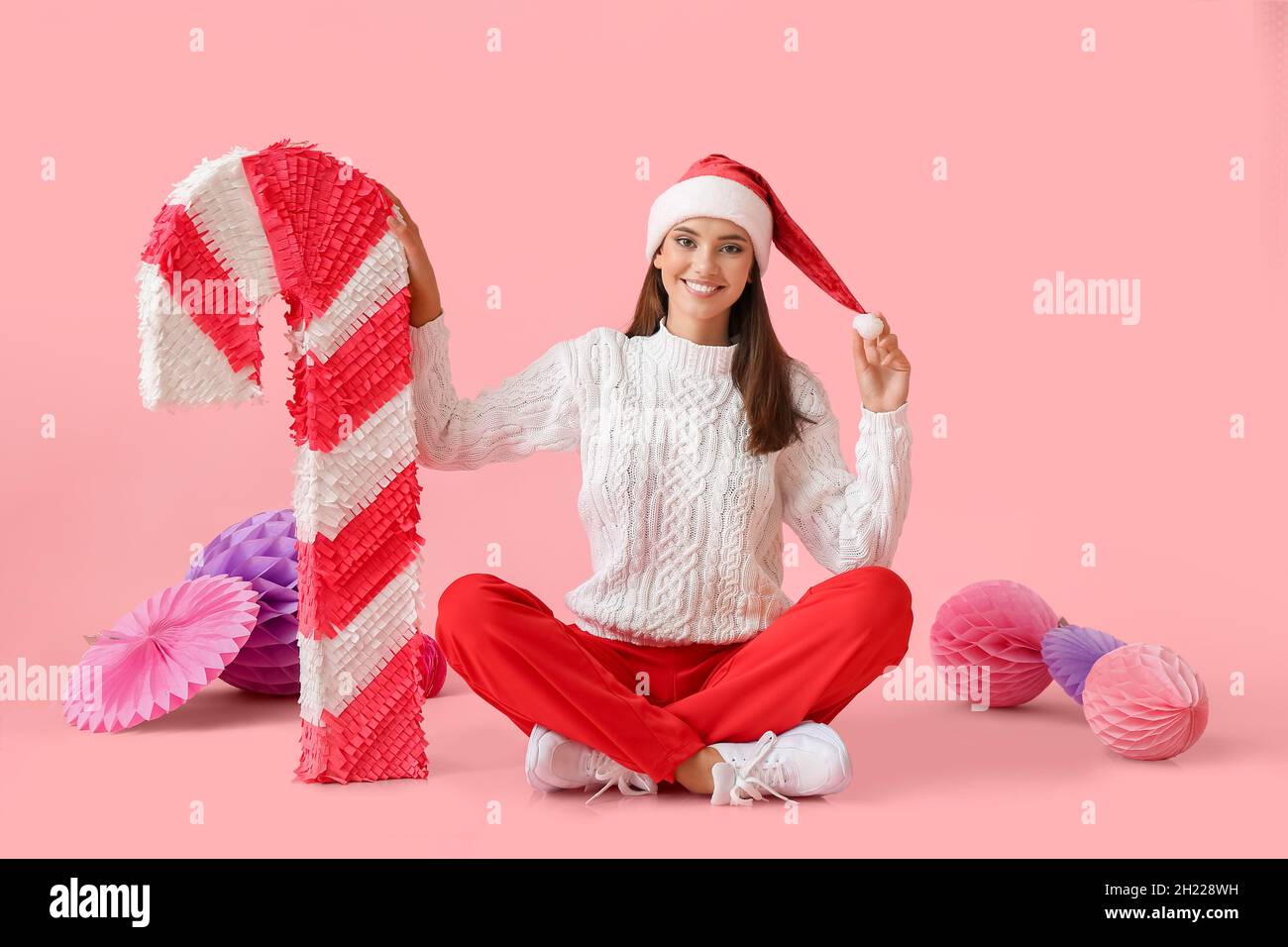 Beautiful woman in Santa hat and with candy cane pinata on color ...