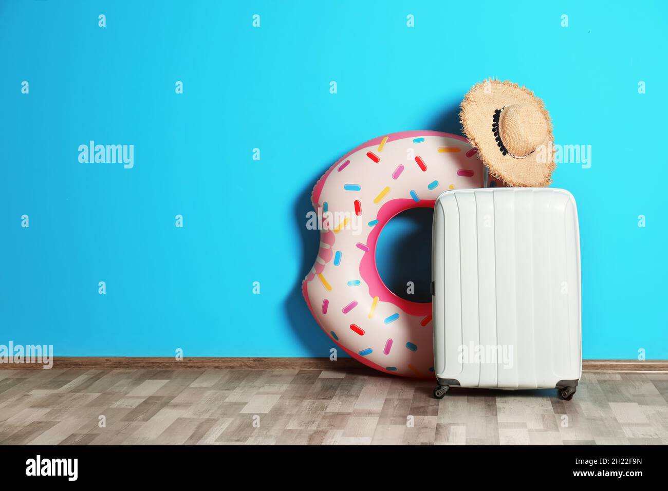 Suitcase with hat and inflatable ring on floor near color wall. Space ...
