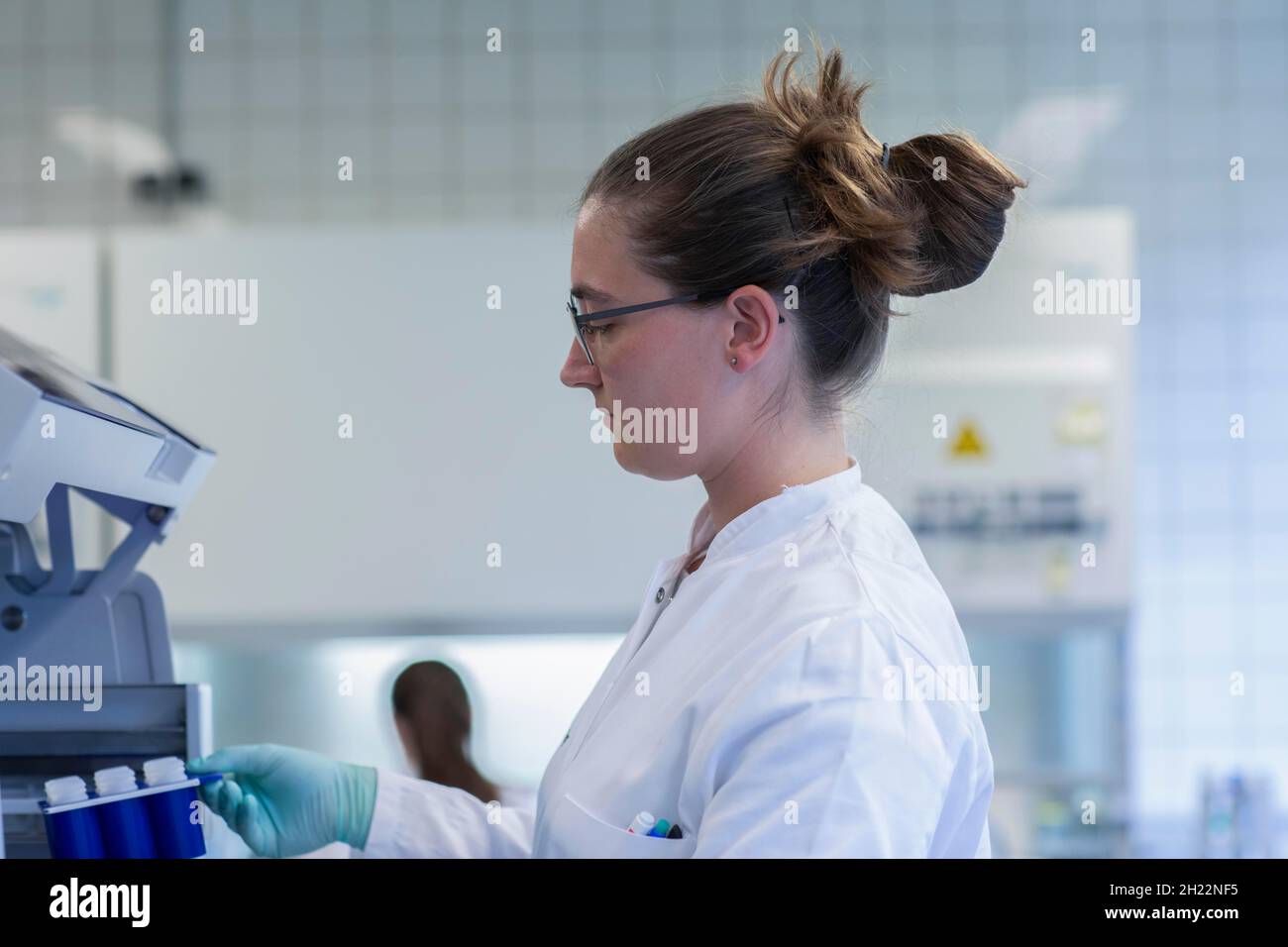Young lab technician wearing a face mask and pipetting a sample in a ...