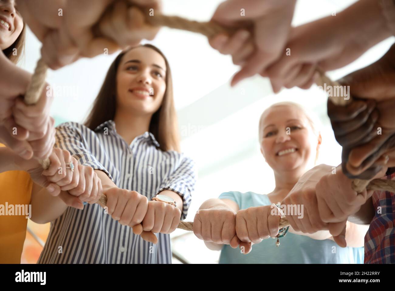 People holding rope together on light background, closeup of hands ...