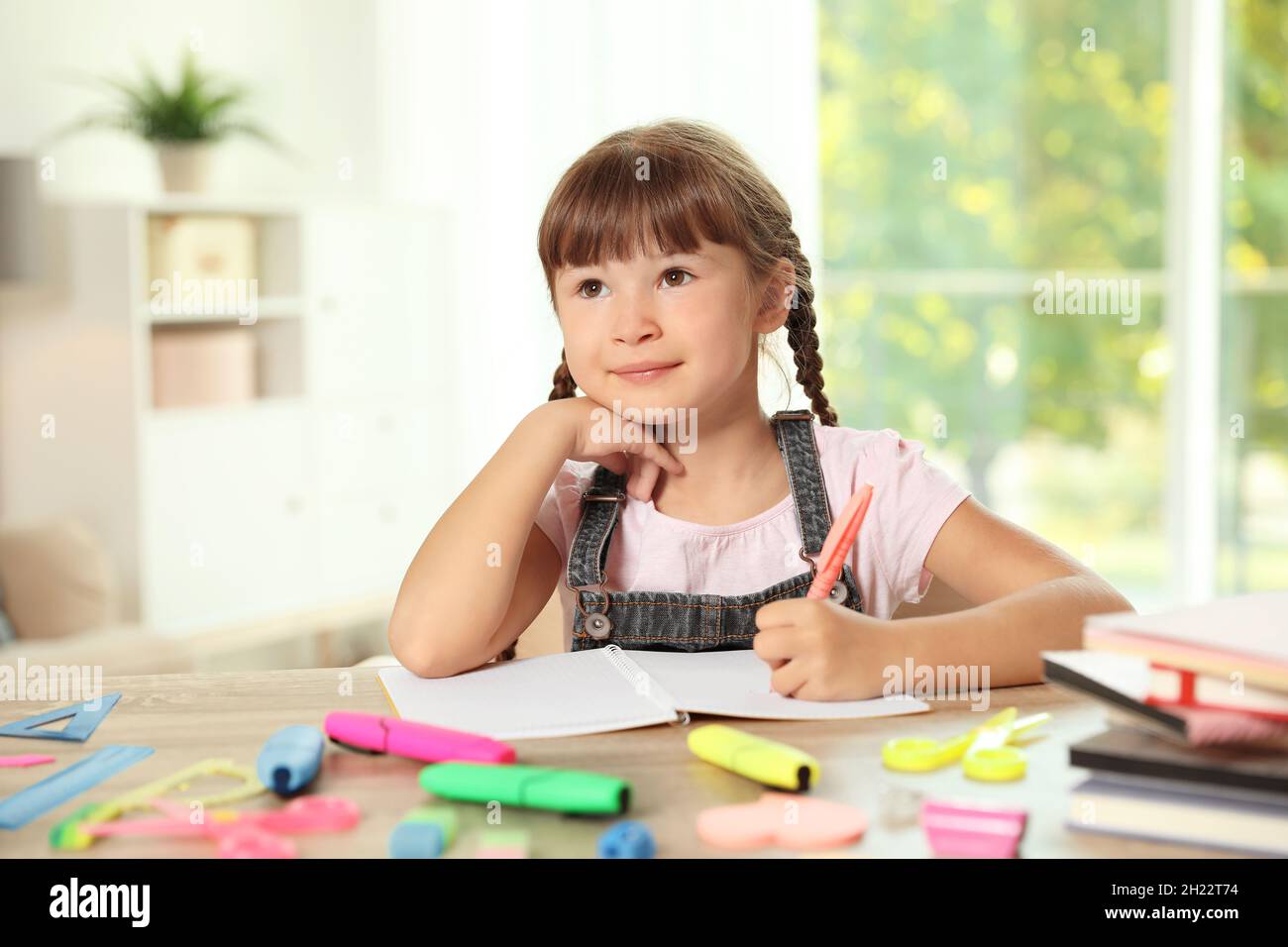 Cute girl doing homework at table with school stationery indoors Stock ...