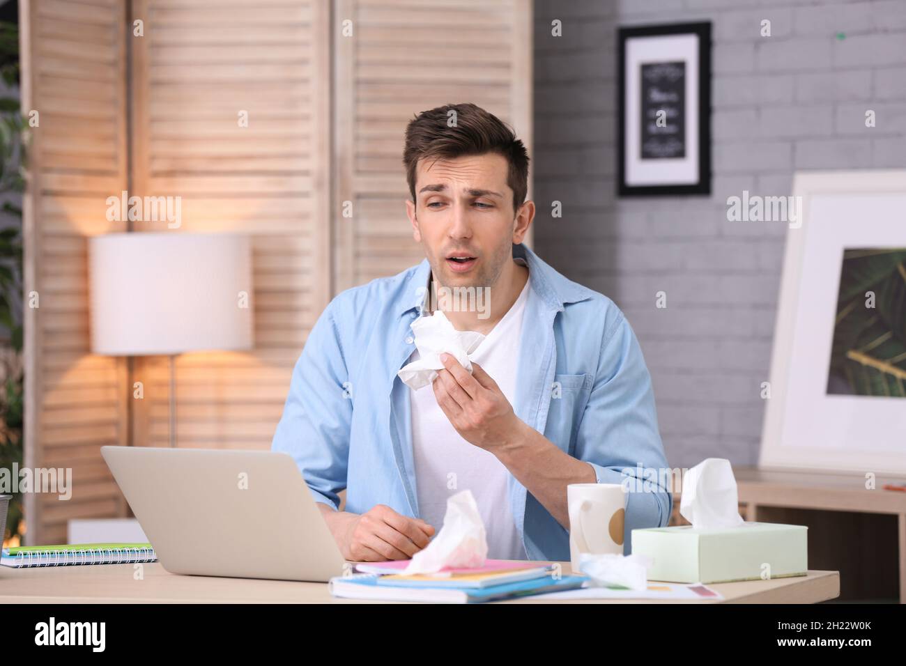 Sad exhausted man with tissue suffering from cold while working with ...