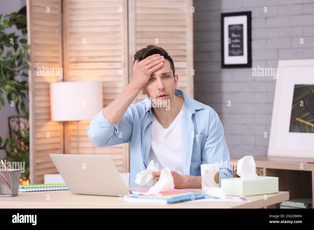 Sad exhausted man with tissue suffering from cold while working with ...