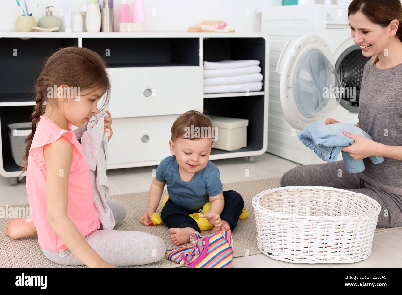 Housewife with children folding freshly washed clothes in laundry room ...
