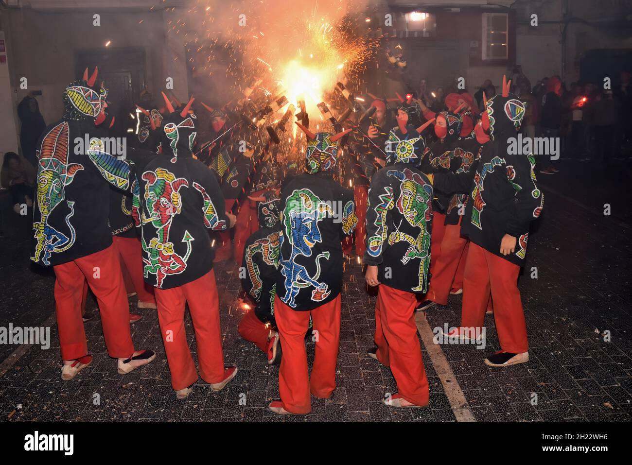 A group of people disguised as devils dance under the sparks of ...