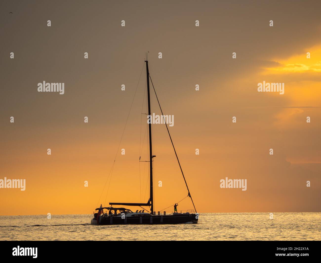 Sailing ship with gathered sails in front of dark clouds, sunset ...