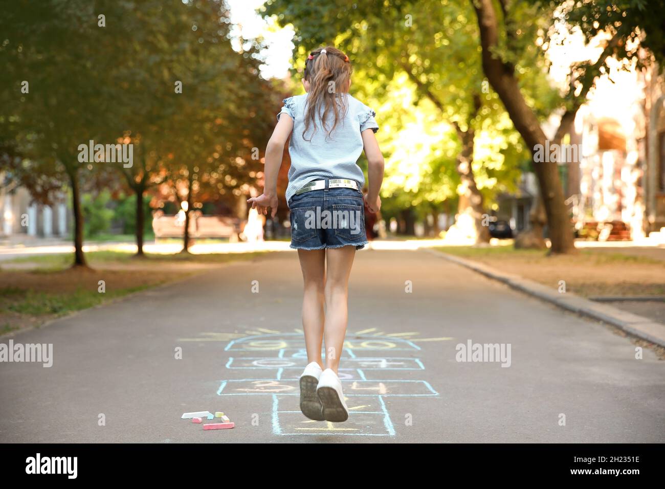 Little child playing hopscotch drawn with colorful chalk on asphalt ...