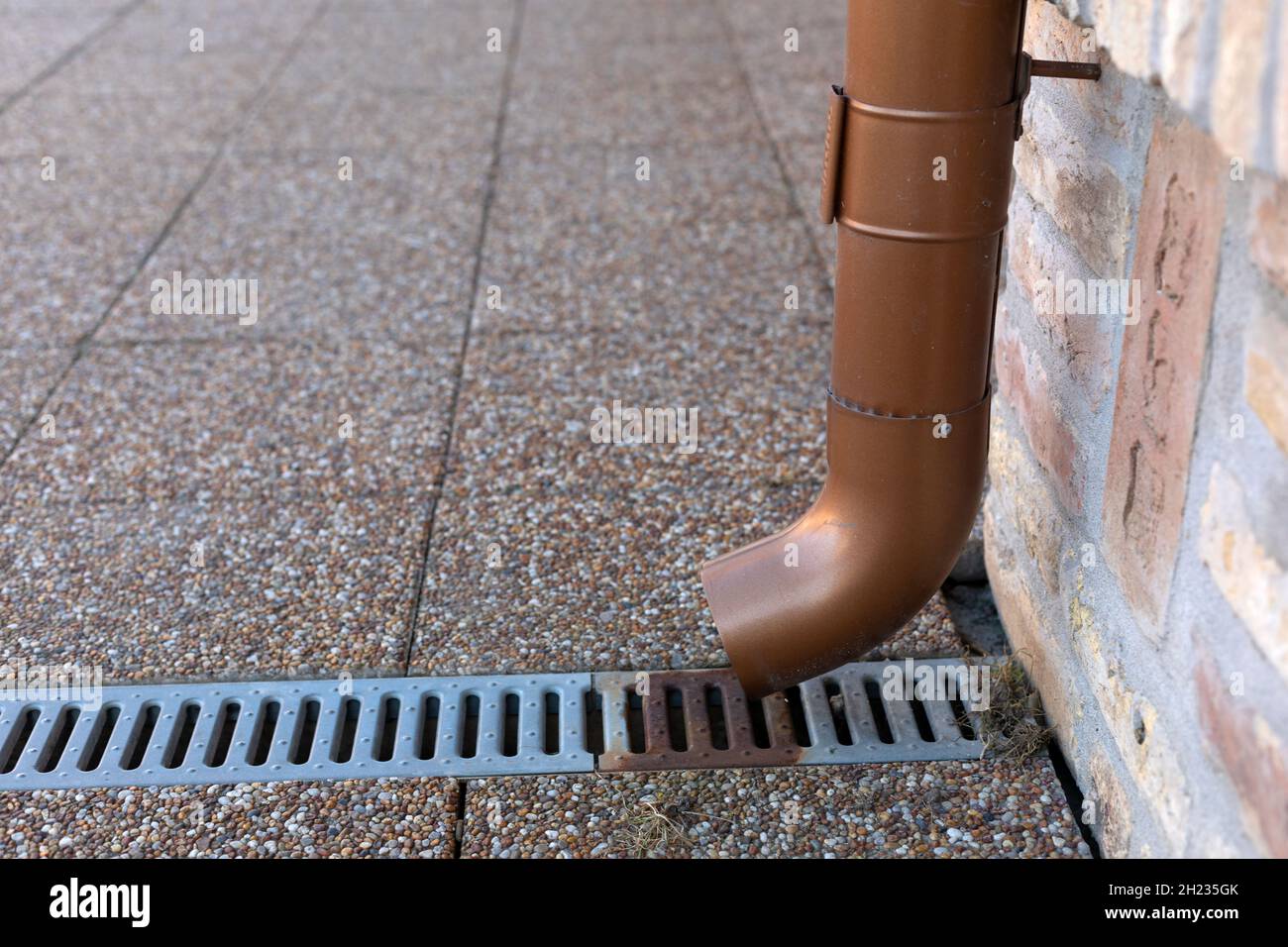 Bronze color metal rainwater downpipe with a drainage grate on a stone ...