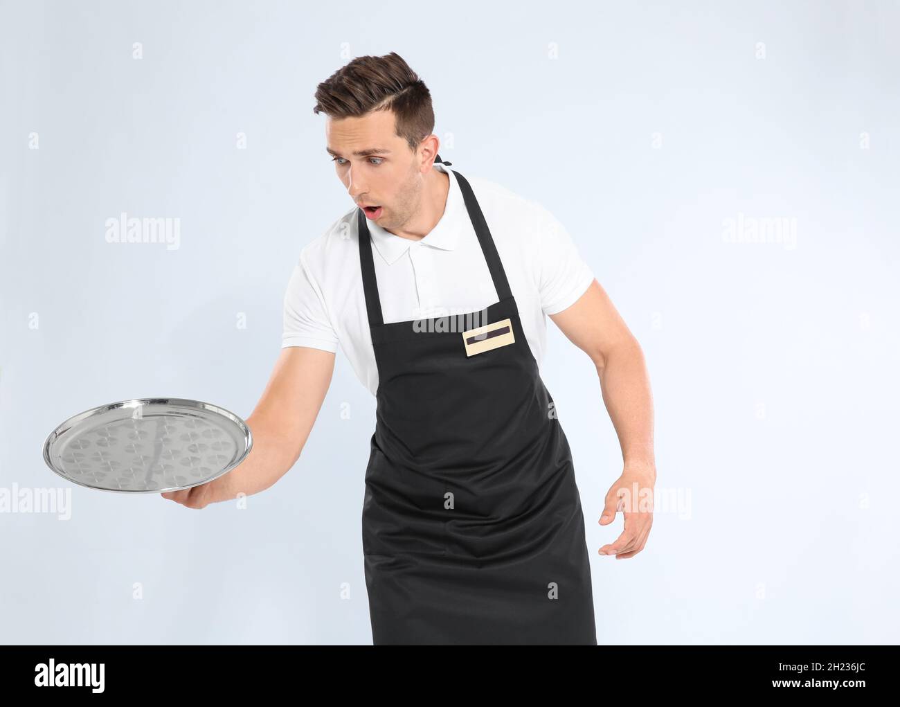 Clumsy waiter dropping empty tray on light background Stock Photo - Alamy
