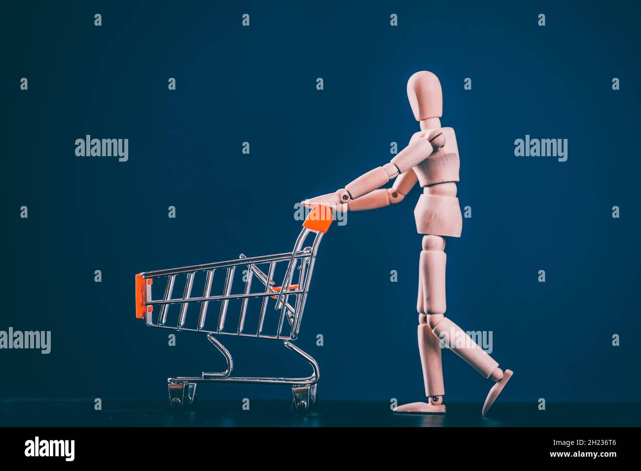 Go shopping concept. Wooden figure with shopping cart on blue ...