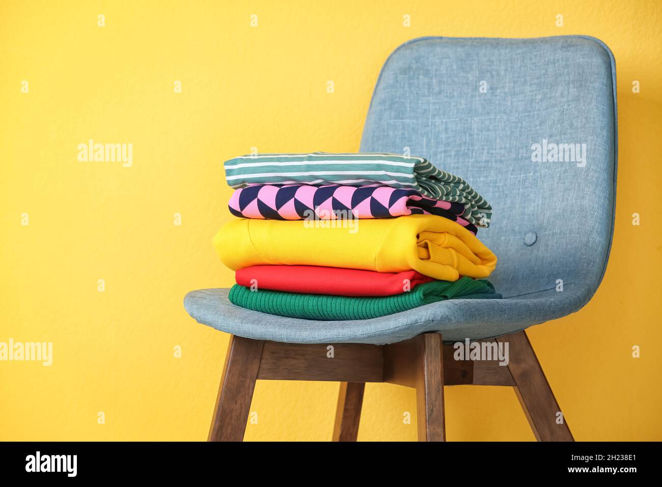 Stack of clothes on chair against color background Stock Photo - Alamy