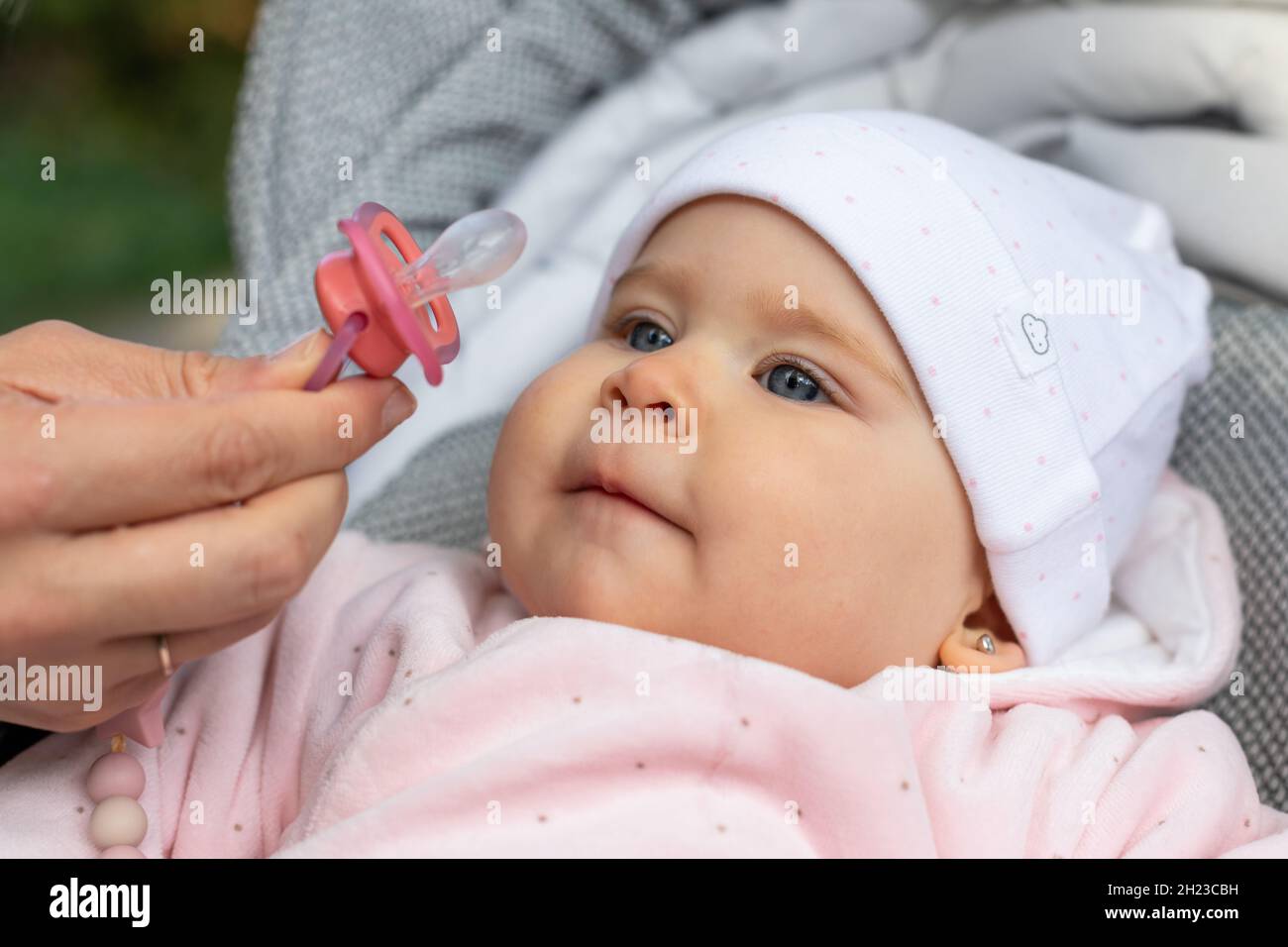 Baby girl with a pacifier in his mouth sitting in a stroller outdoor ...