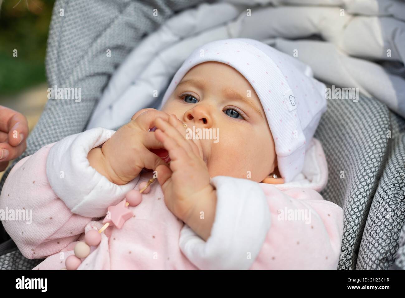 Baby girl with a pacifier in his mouth sitting in a stroller outdoor ...
