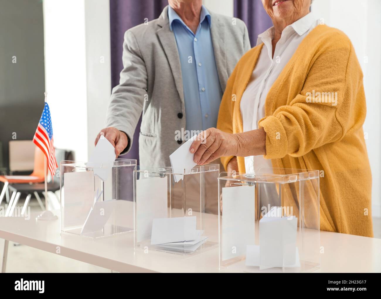 Elderly people putting ballot papers into boxes at polling station ...