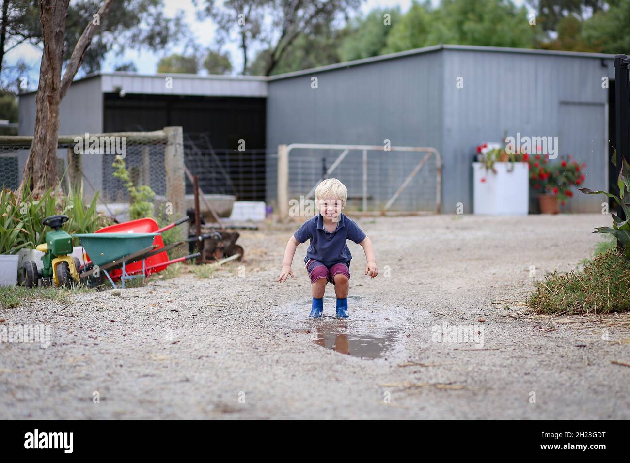 Little boy wearing gum boots jumping and splashing in puddle after rain ...