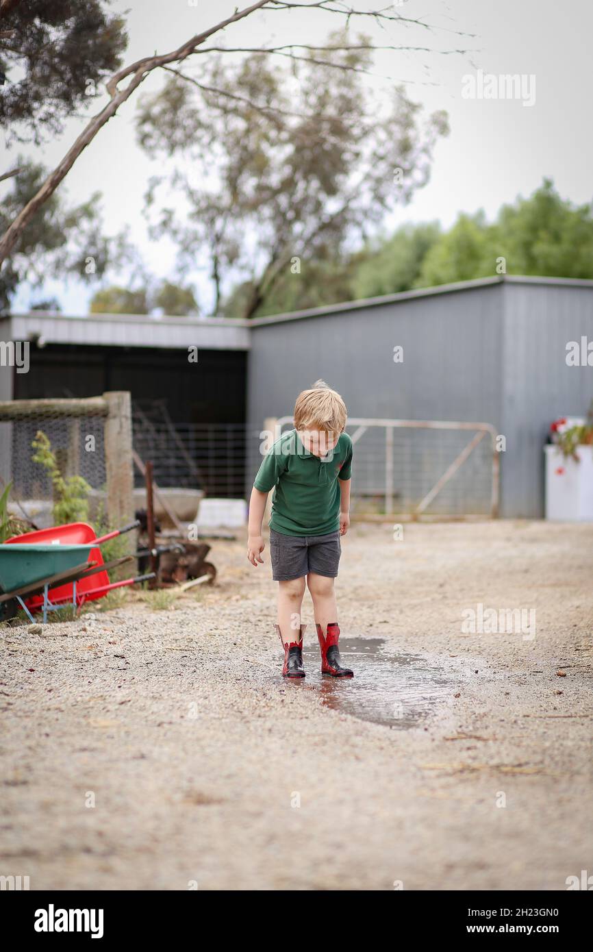 Little boy wearing gum boots jumping and splashing in puddle after rain ...