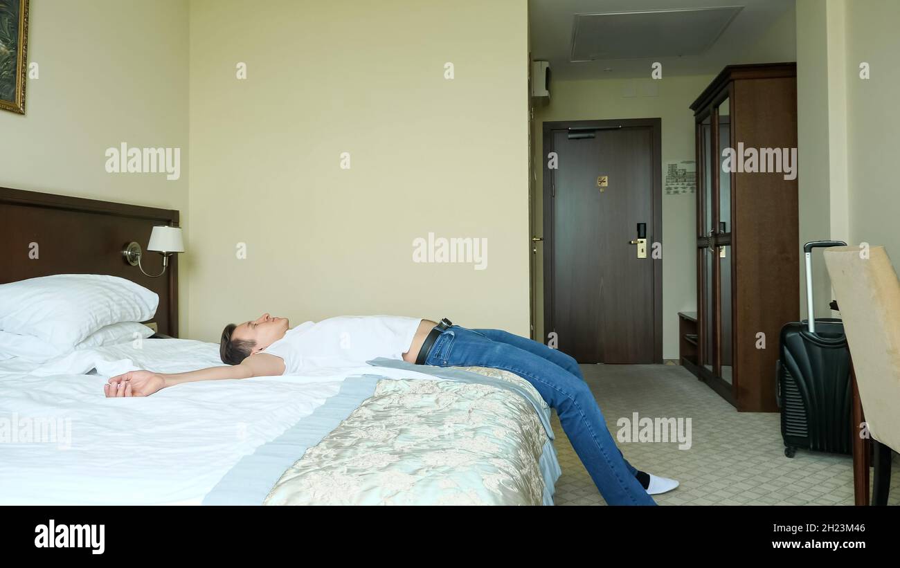 young man with a suitcase enters the hotel room and falls contentedly ...