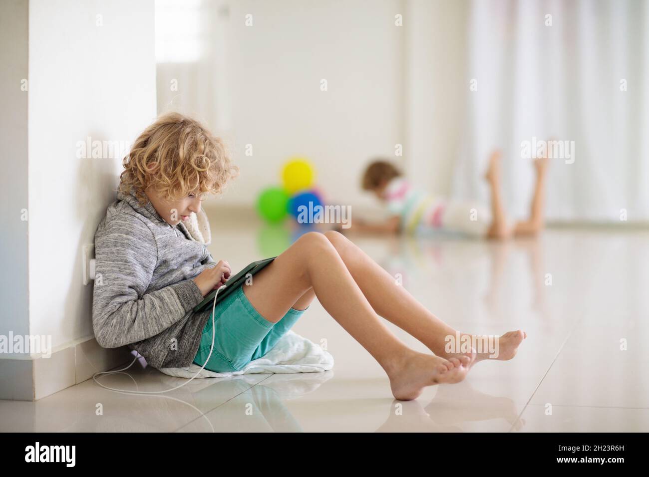 Kid with tablet computer. Child playing game on tile floor in white ...