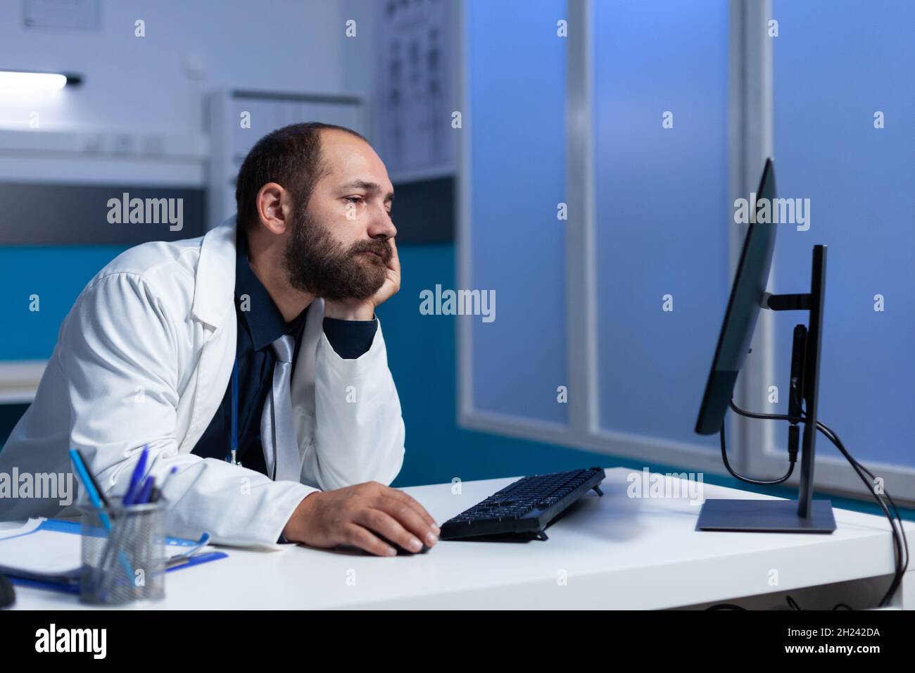 Tired physician working late at night with monitor for medical checkup ...
