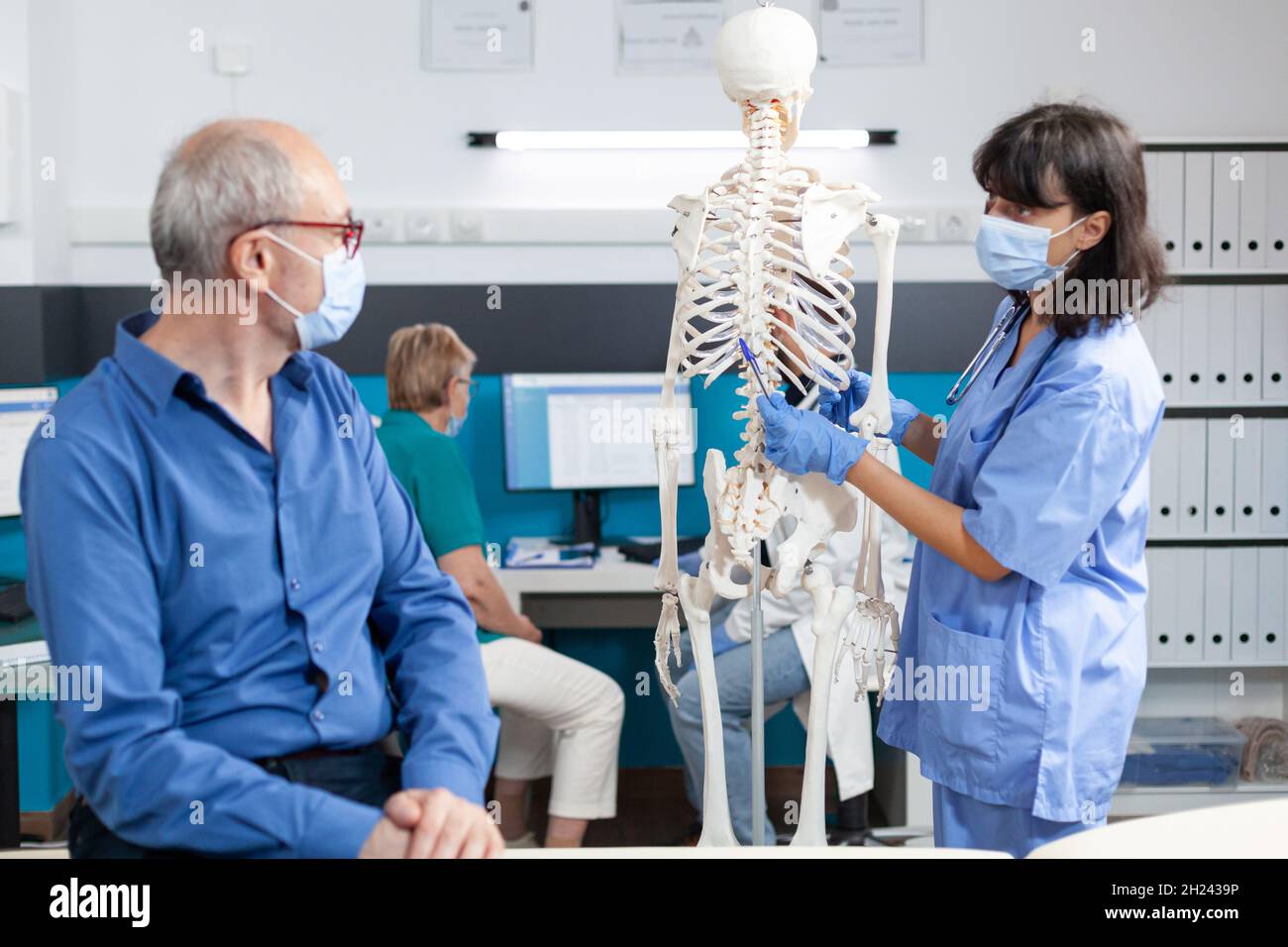 Retired man looking at human skeleton for chiropractic care. Assistant ...