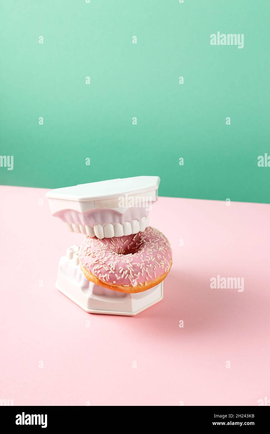 Plastic jaws hold sweet pink donut in teeth. Dental health, dentistry ...