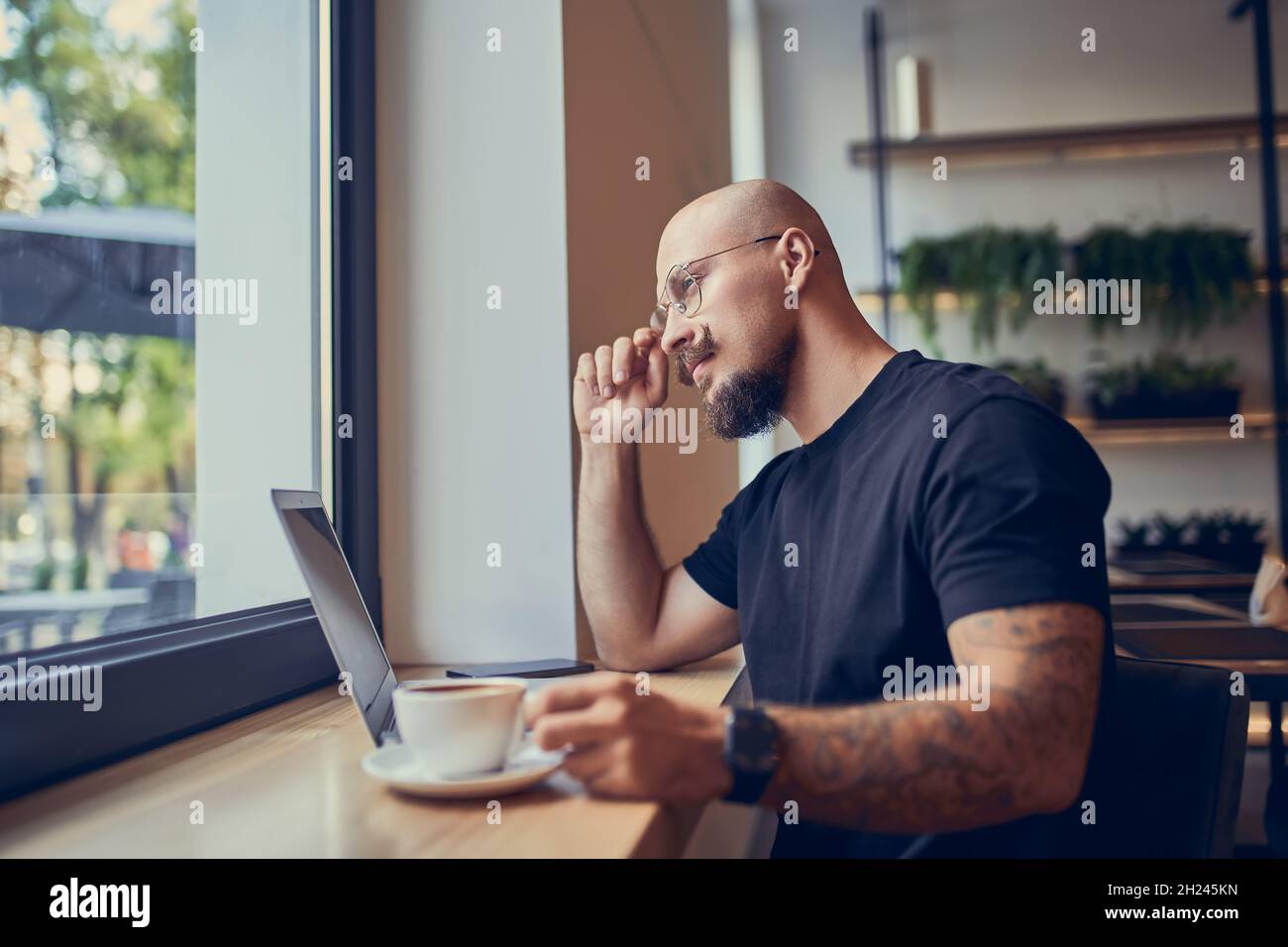 Serious hipster millennial man works at laptop while sits in cafe with ...