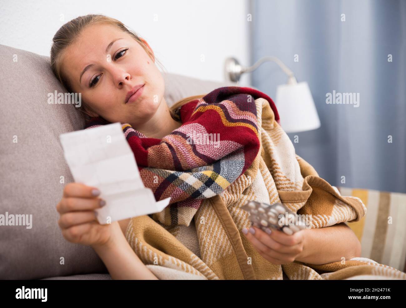 Sick woman lying at home on cozy sofa with plaid and reading recipe ...