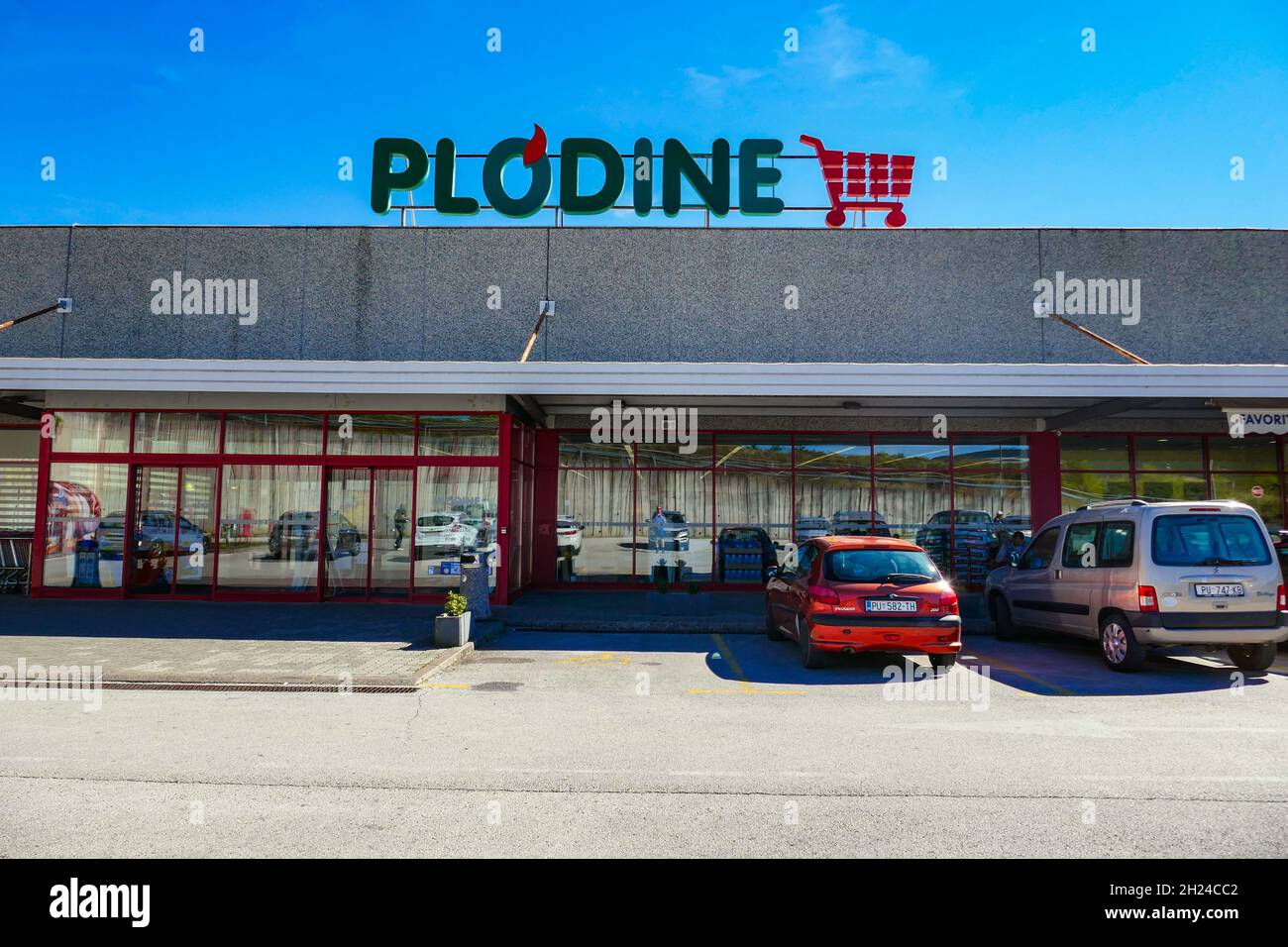 Cars parked outside Plodine, Croatian supermarket near the ancient hill ...