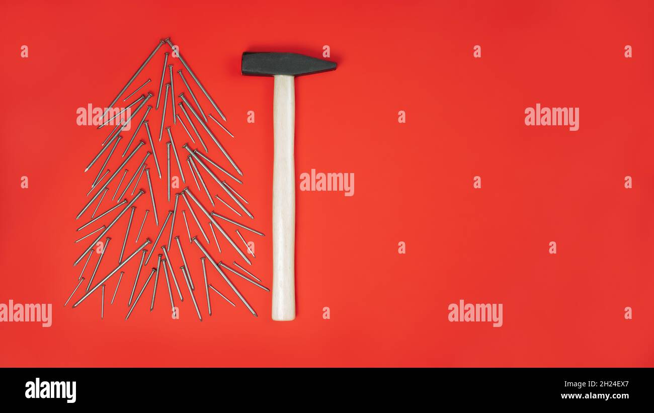 Long nails and hammer, laid out in shape of Christmas tree on red ...